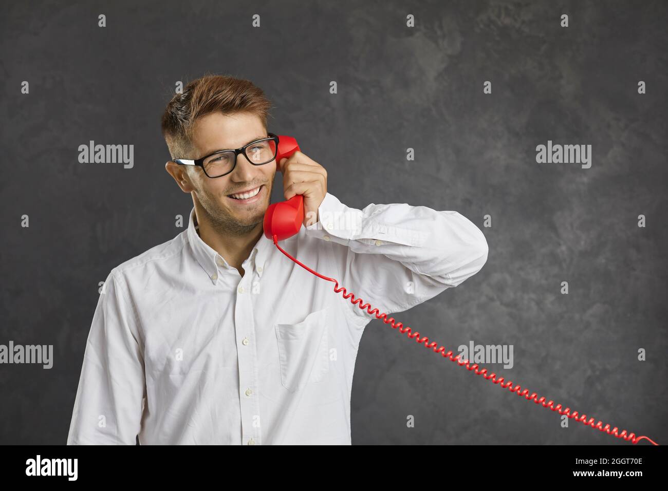 Studio portrait of a happy young man talking on red landline telephone ...