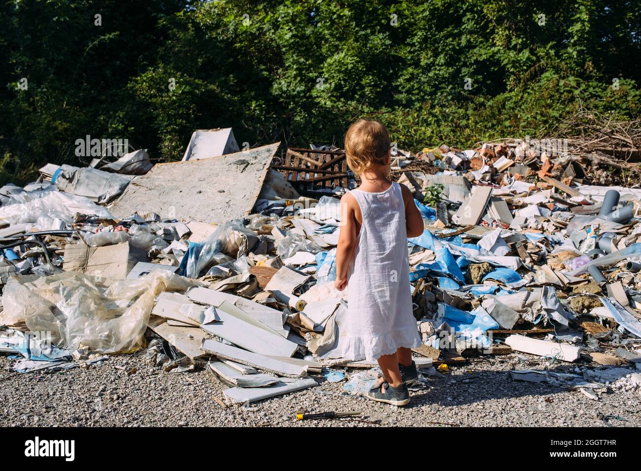 Little girl at a dump among a heap of scattered garbage in the forest ...