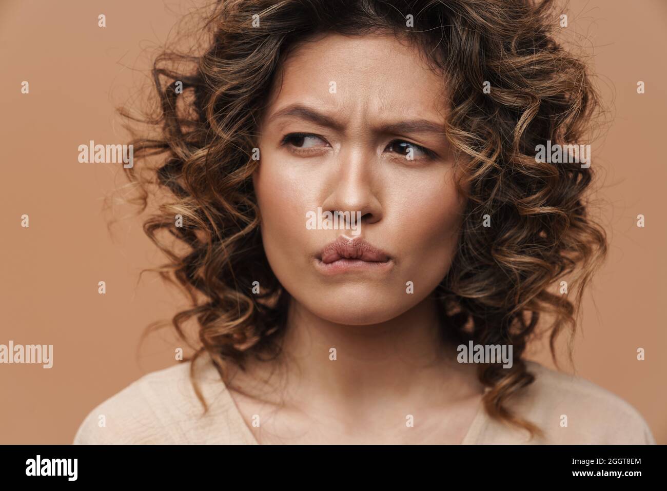 Young curly hispanic woman frowning and looking aside isolated over ...