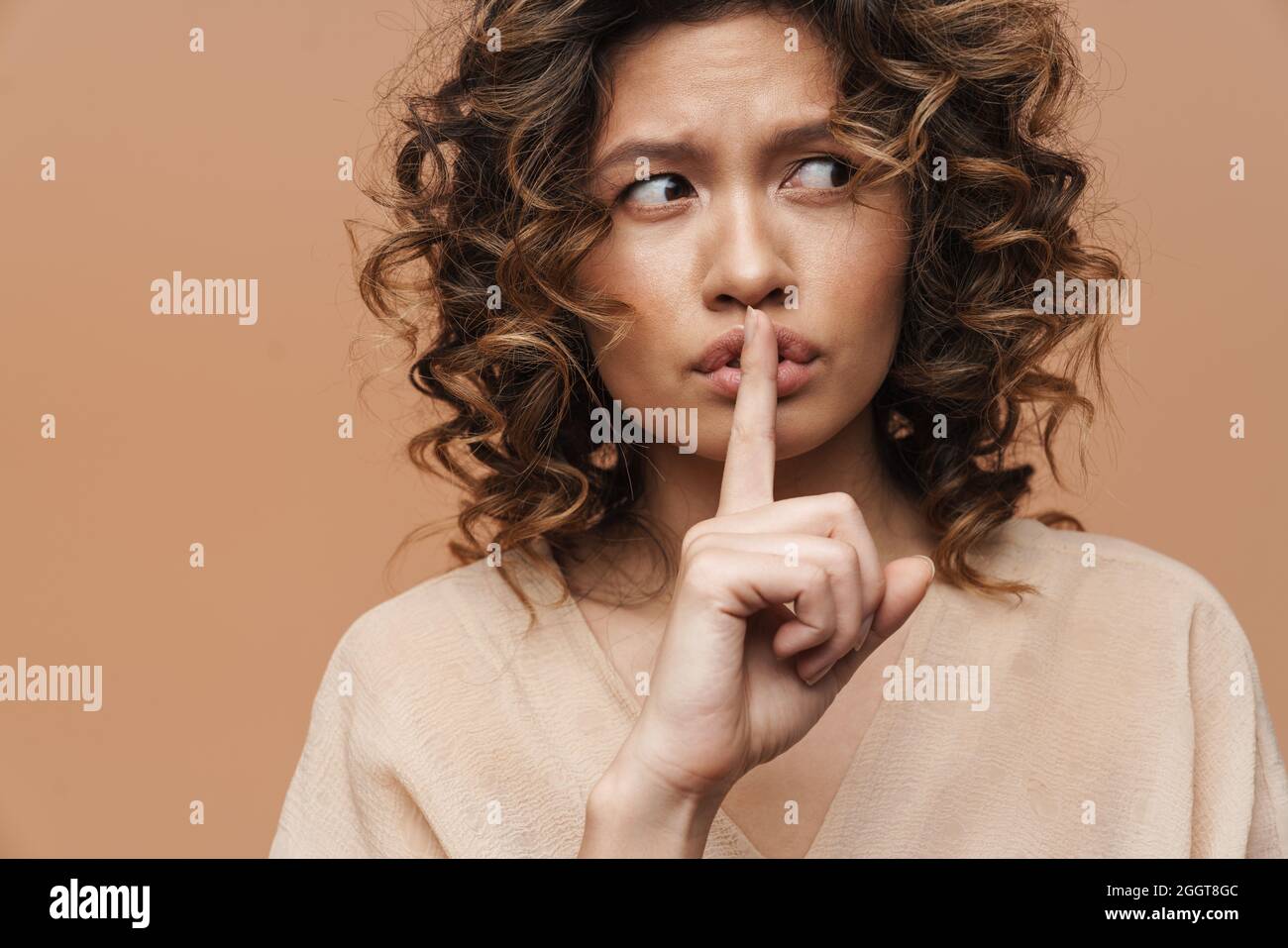 Young hispanic woman frowning while showing silence gesture at camera ...