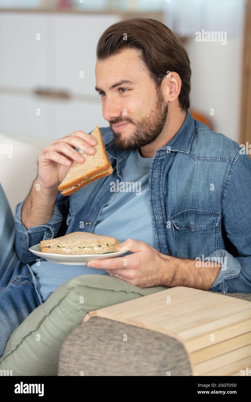 young man eating sandwich on his sofa Stock Photo - Alamy