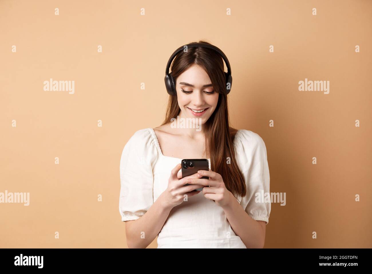 Smiling woman texting message on phone and listening music in wireless ...