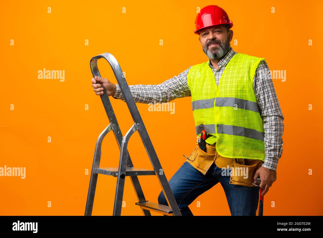 Handyman in uniform standing with ladder against orange background ...