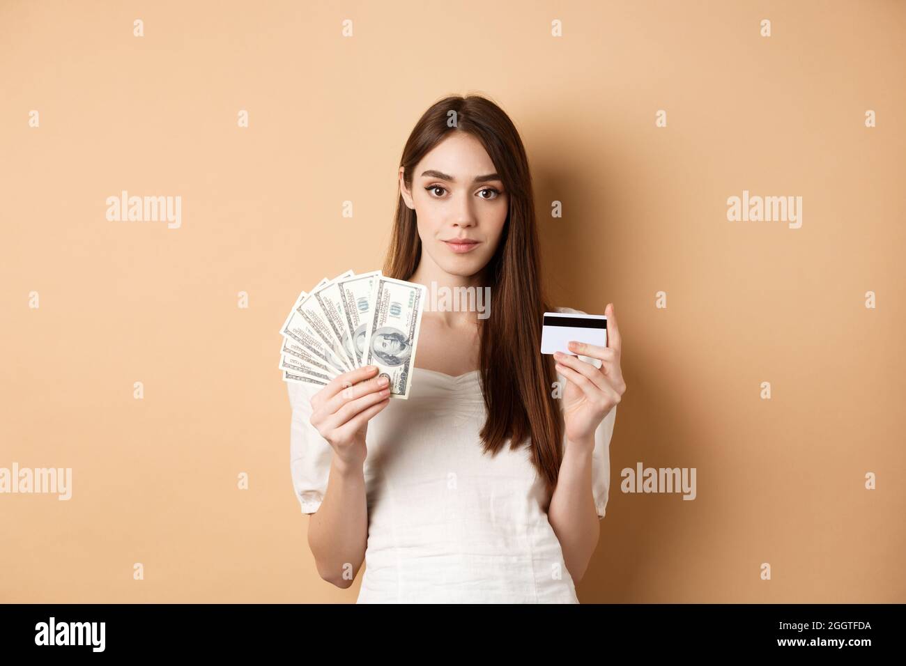 Pretty young woman in white blouse showing dollar bills and plastic credit card, contactless ...