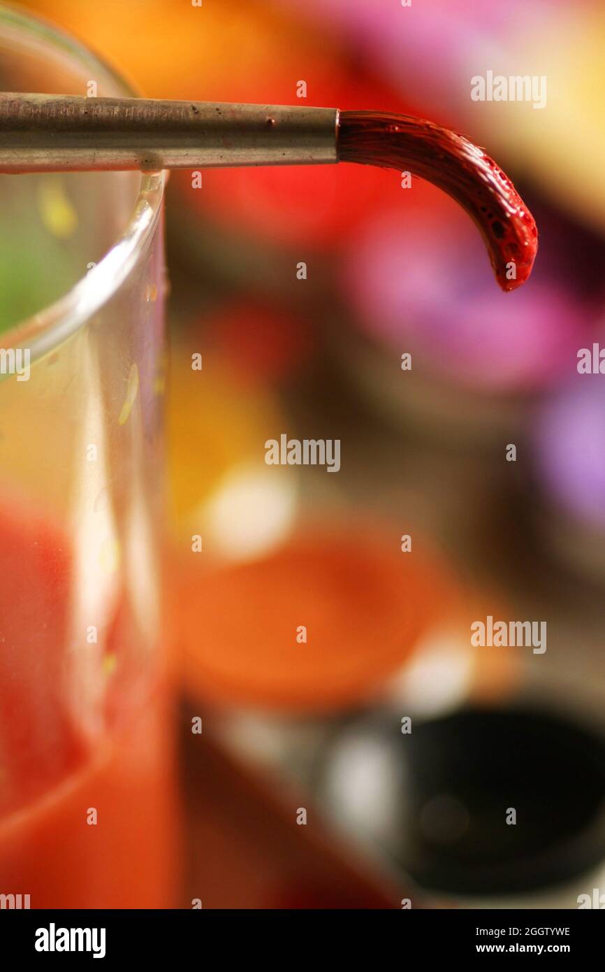 used paint-brush with red paint on a water glass, paint box in the ...