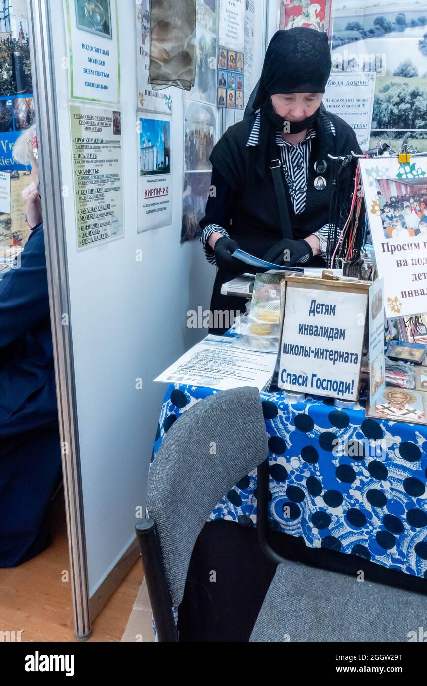 Female church worker in black uniform at the stand at Orthodox fair ...