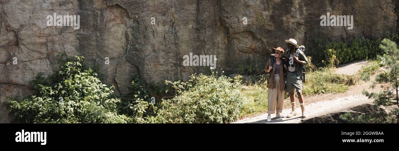 African american hiker standing near senior wife and cliff, banner ...