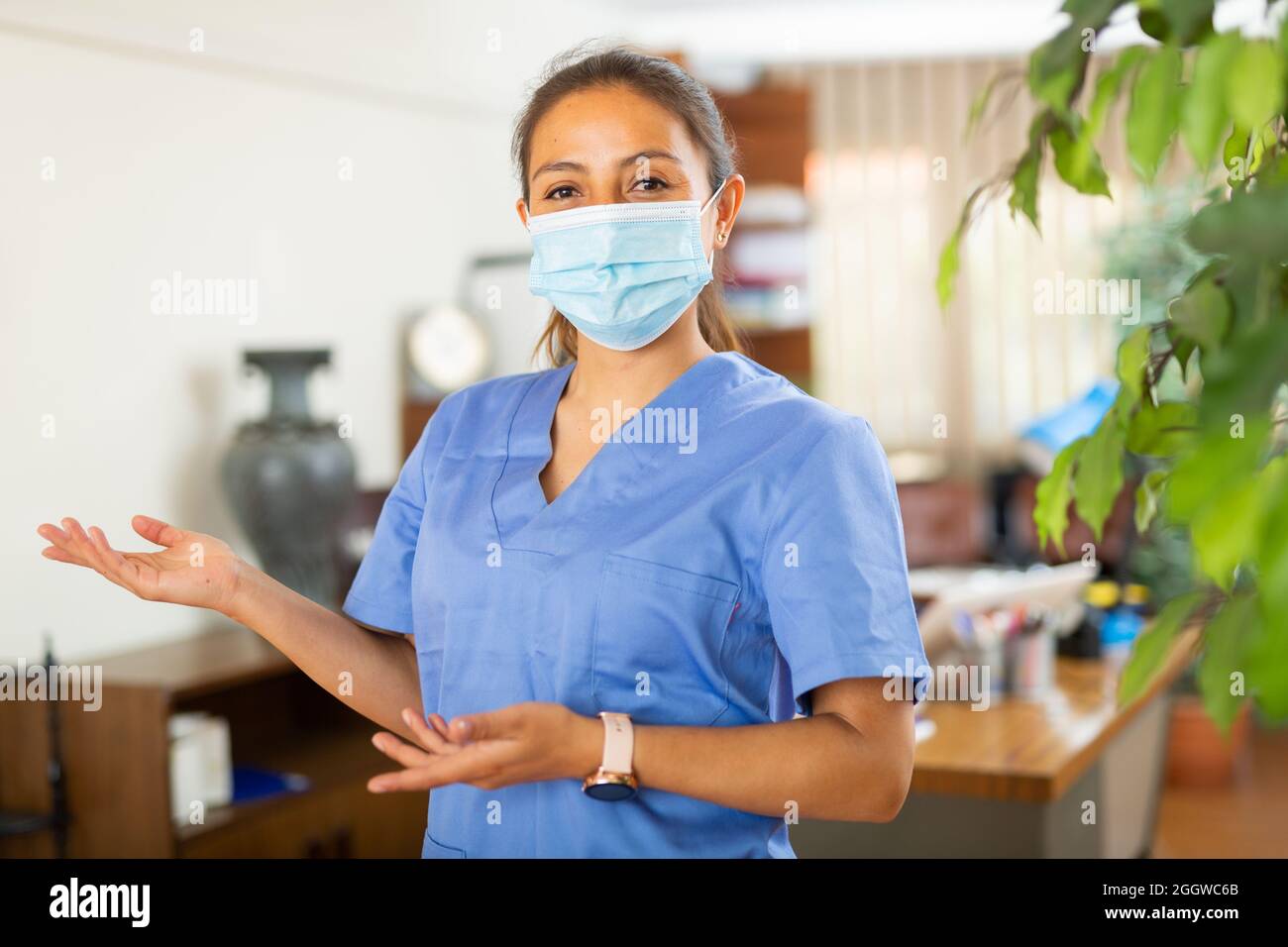 Female health worker in blue uniform and mask welcoming to clinic Stock ...