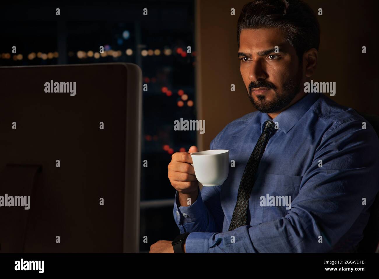 An employee holding coffee mug sitting with intense look in office at ...