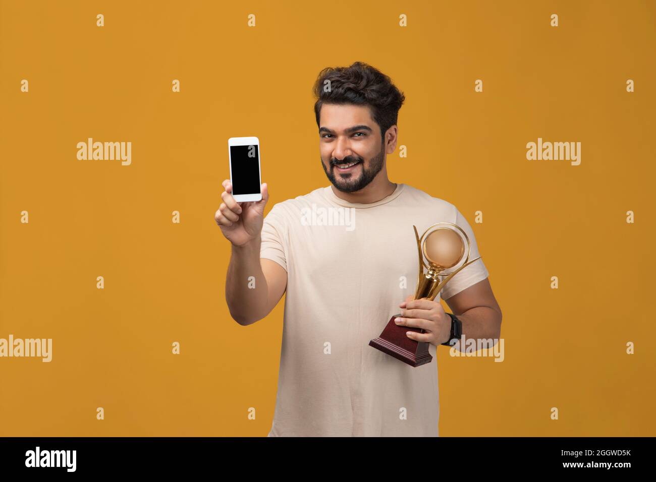 Portrait of a man with a trophy showing mobile phone against plain ...