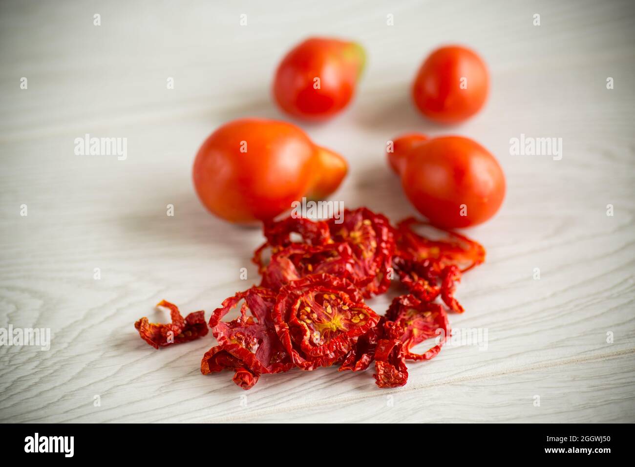 a handful of dried tomatoes and fresh tomatoes on a light table Stock ...