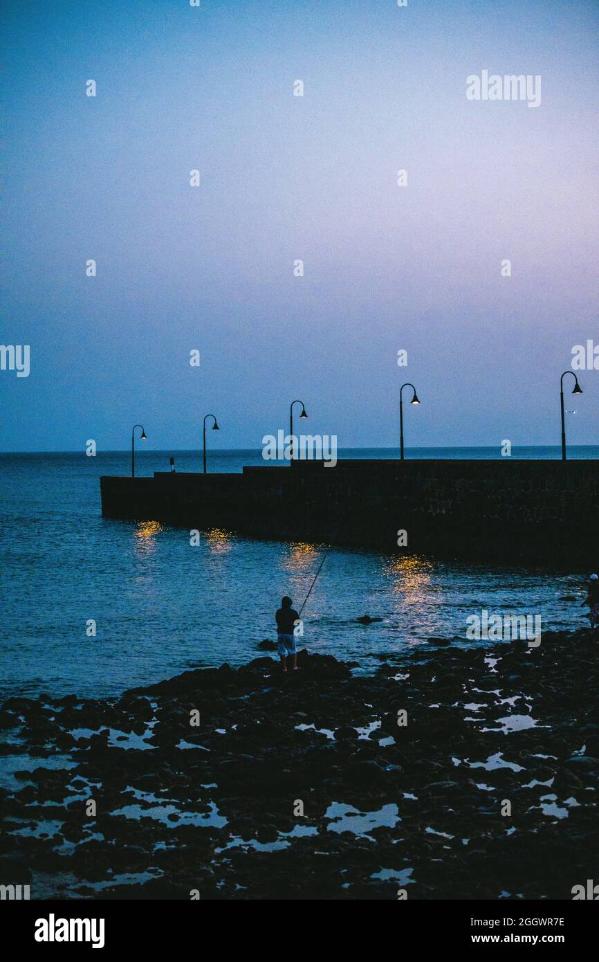 Man with a fishing rod standing on the rocks near the sea in the ...