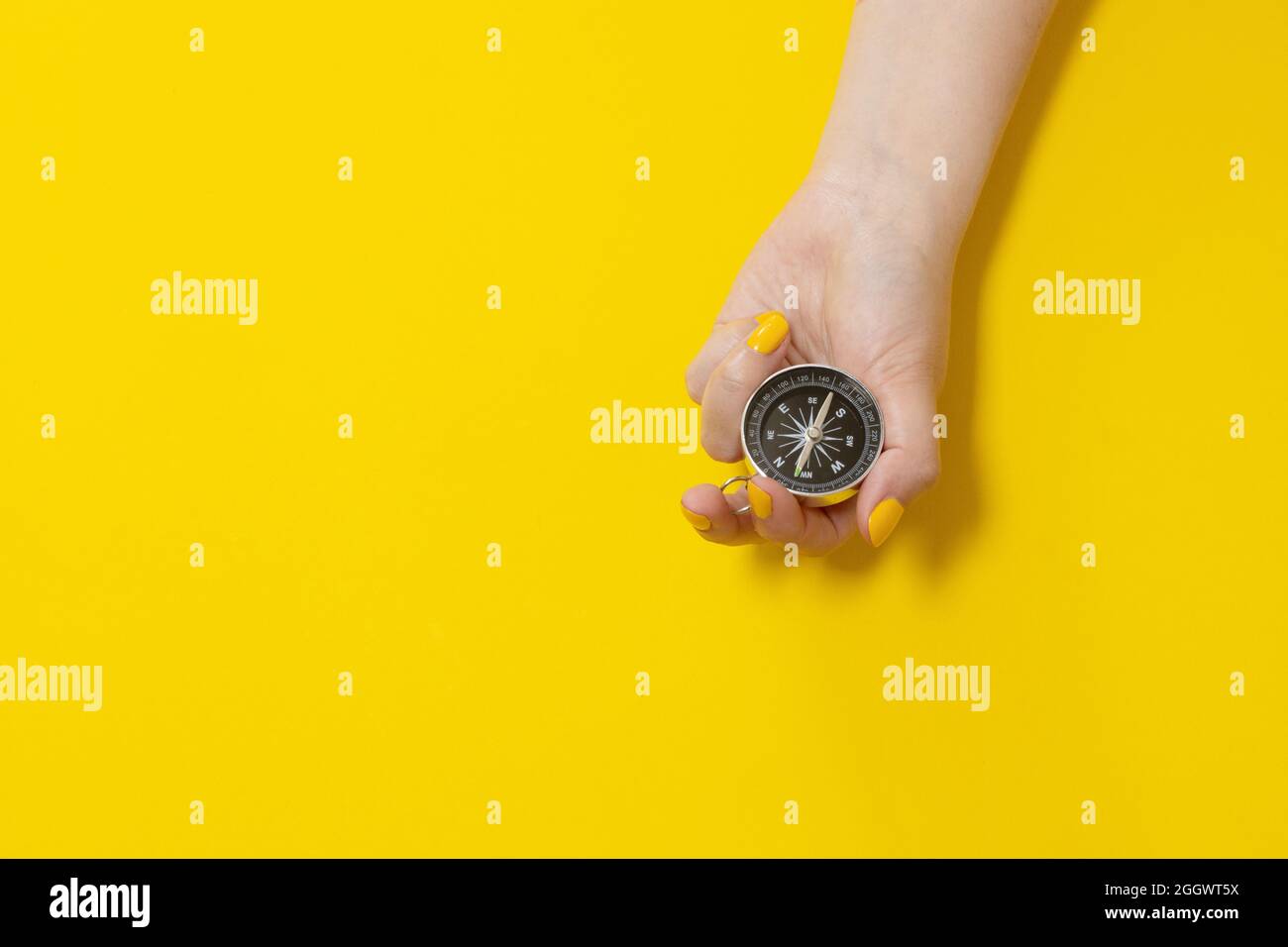 Female hand holding a compass on a yellow background with copy space ...