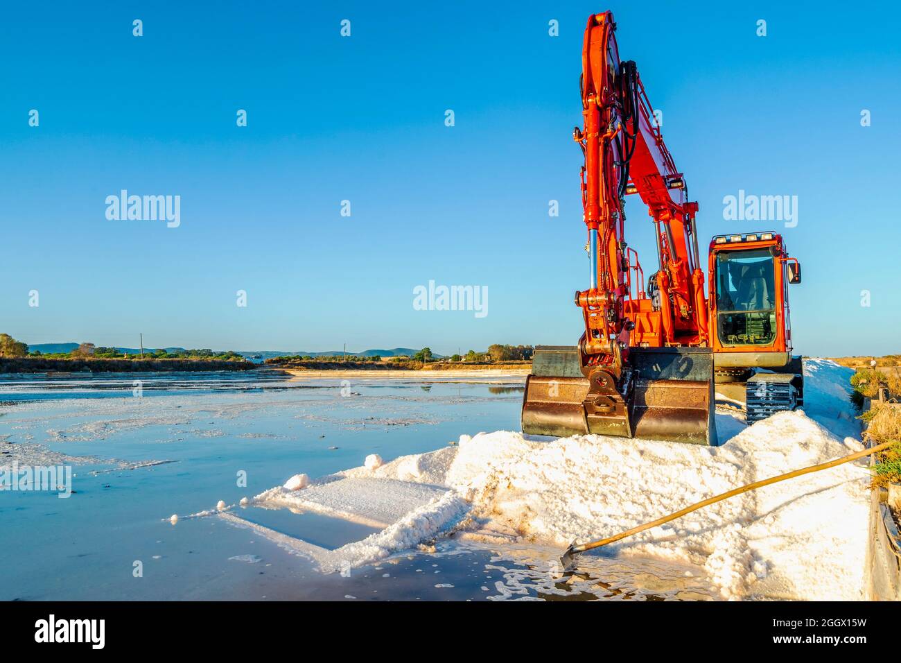 Red bulldozer harvesting sea salt from pond and making a heap of salt ...