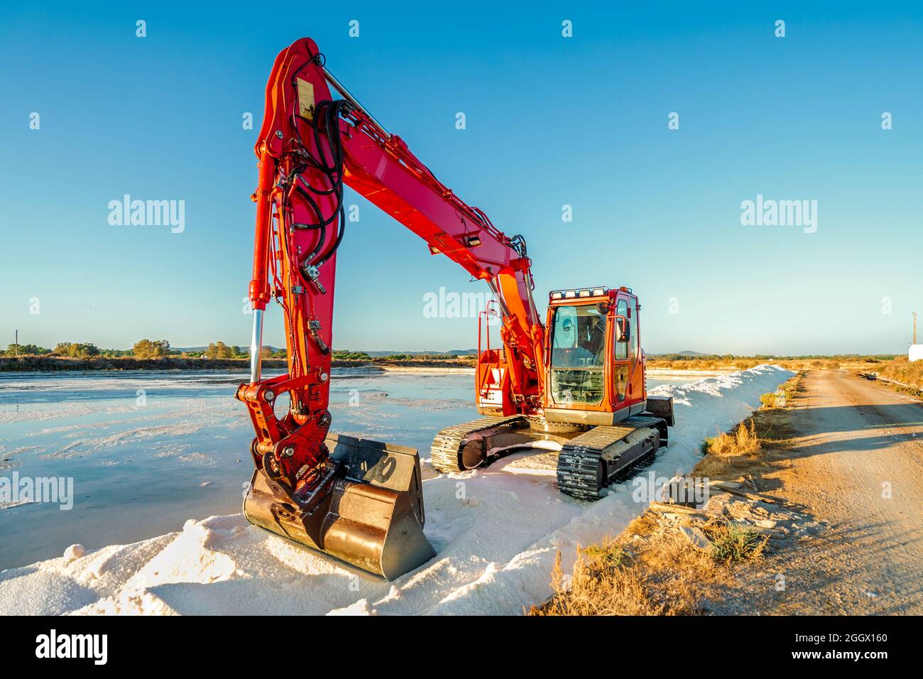 Red bulldozer harvesting sea salt from pond and making a heap of salt ...