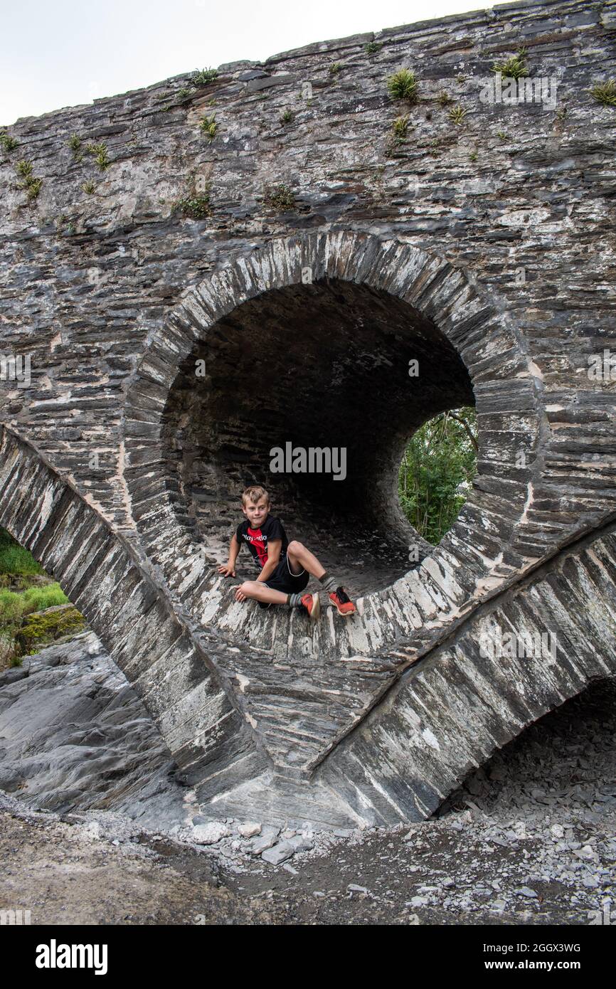 Boy in a cylindrical hole on the road bridge in the village of Cenarth ...