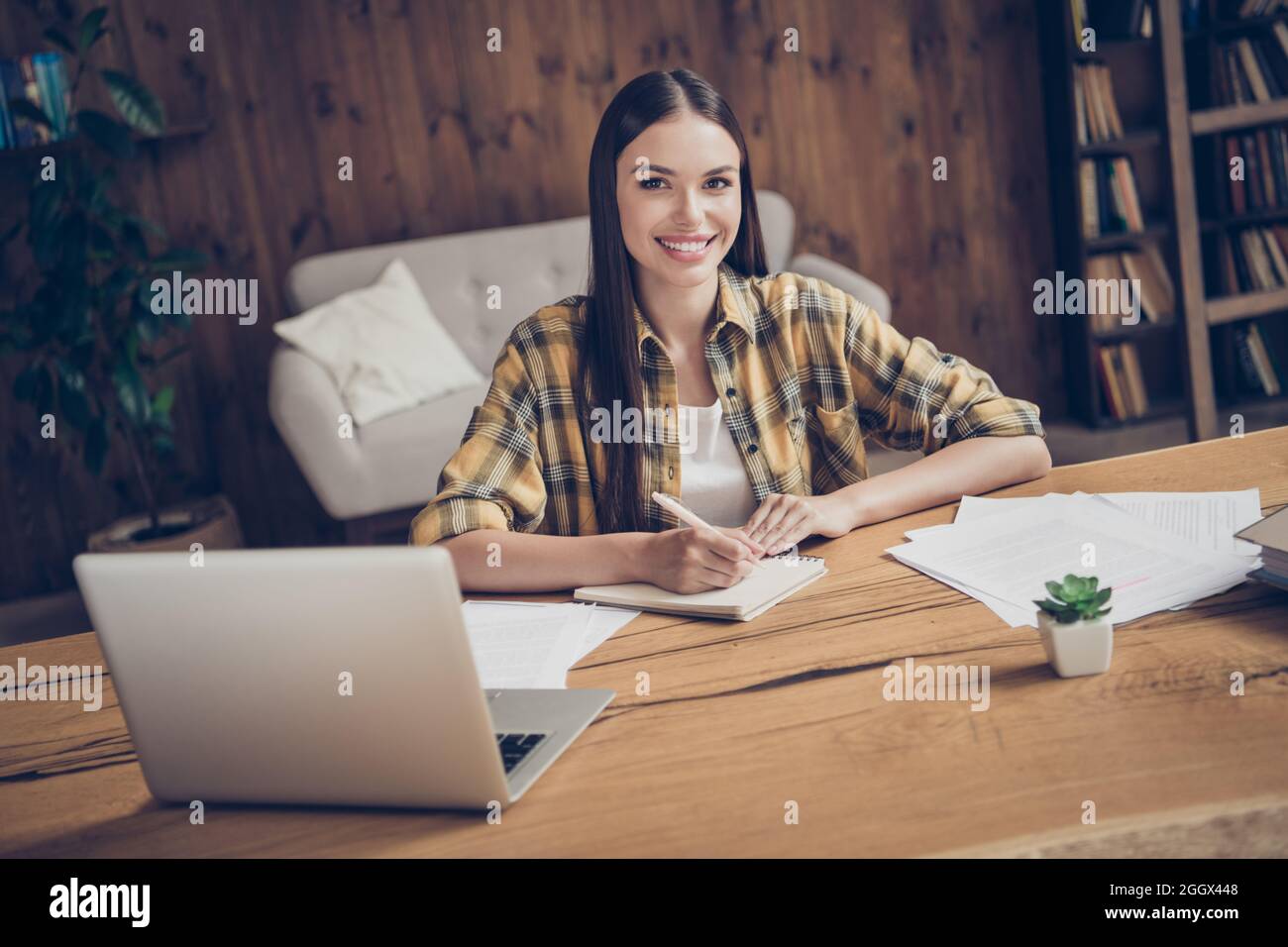 Portrait of attractive cheerful girl sitting in public library writing ...