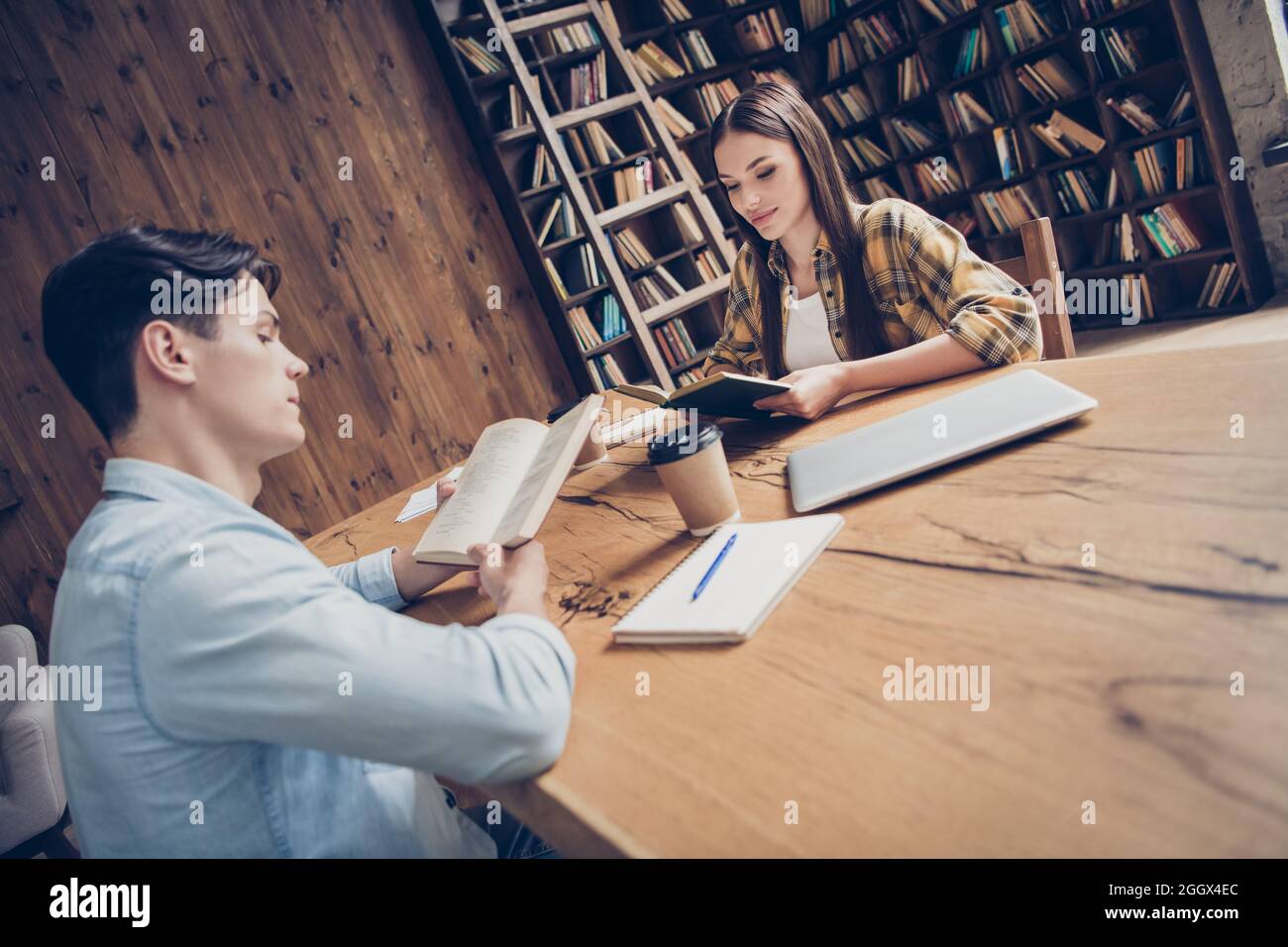 Portrait of two attractive focused people learners reading paper book ...