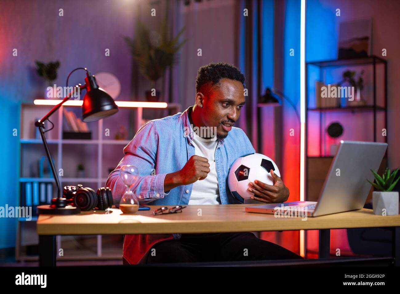 Worried african guy in denim shirt using wireless laptop for watching ...