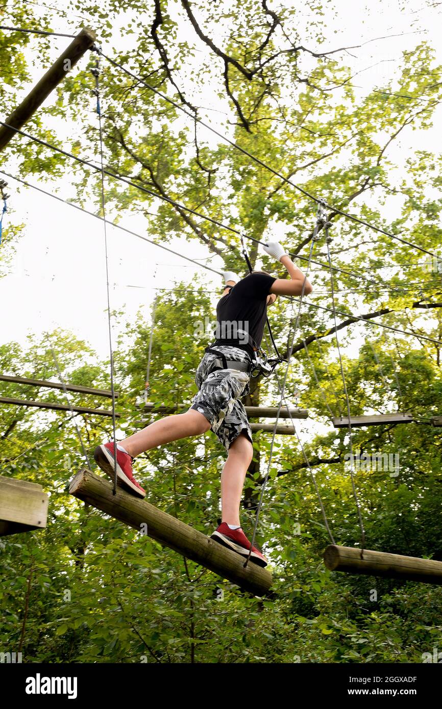 Young guy runs an obstacle course from tree to tree on a rope park ...