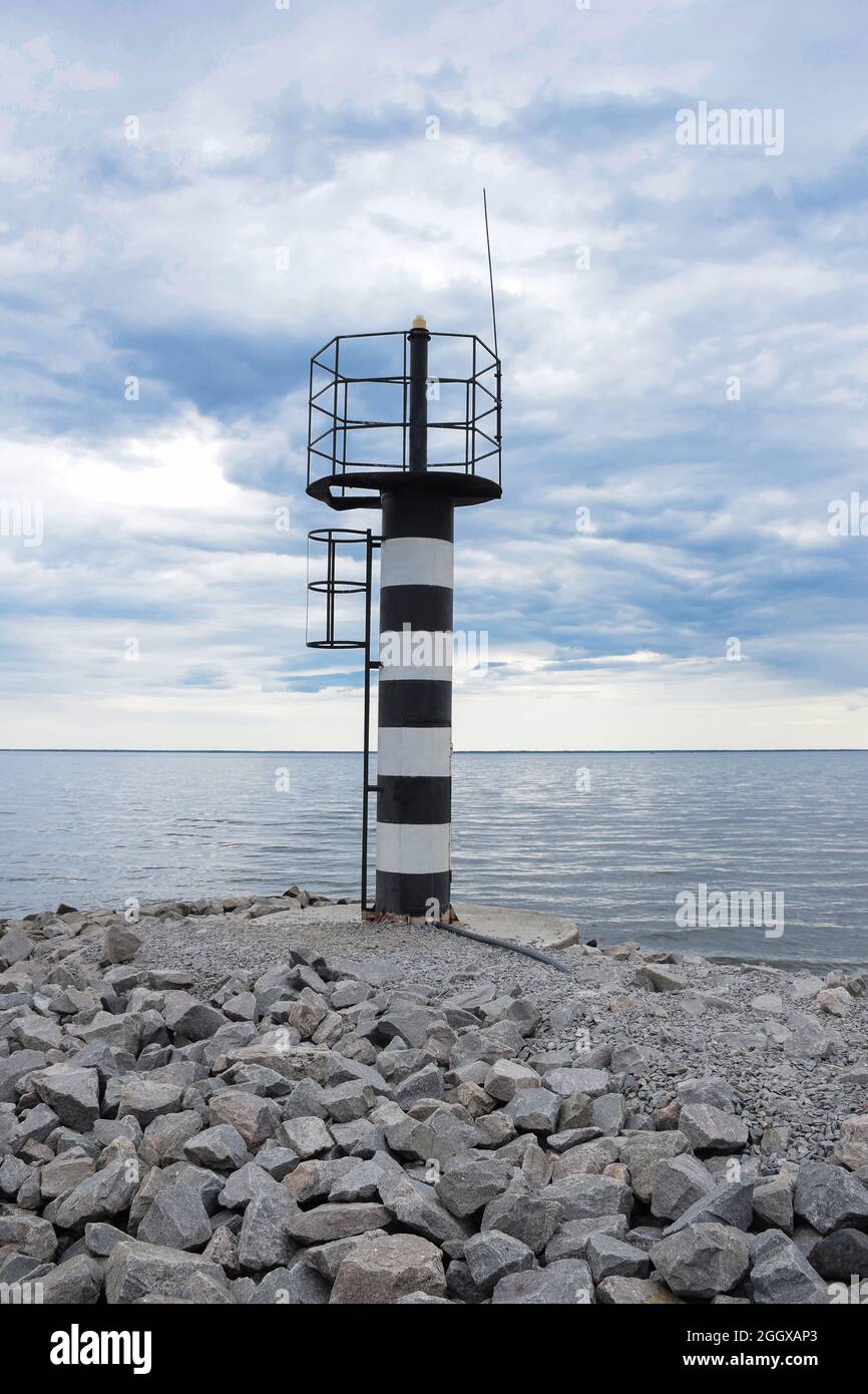 A small iron lighthouse on the seashore, strewn with stones, against a ...