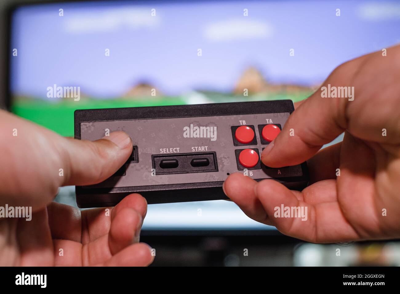 A man's hands hold an old-fashioned game console controller in front of ...