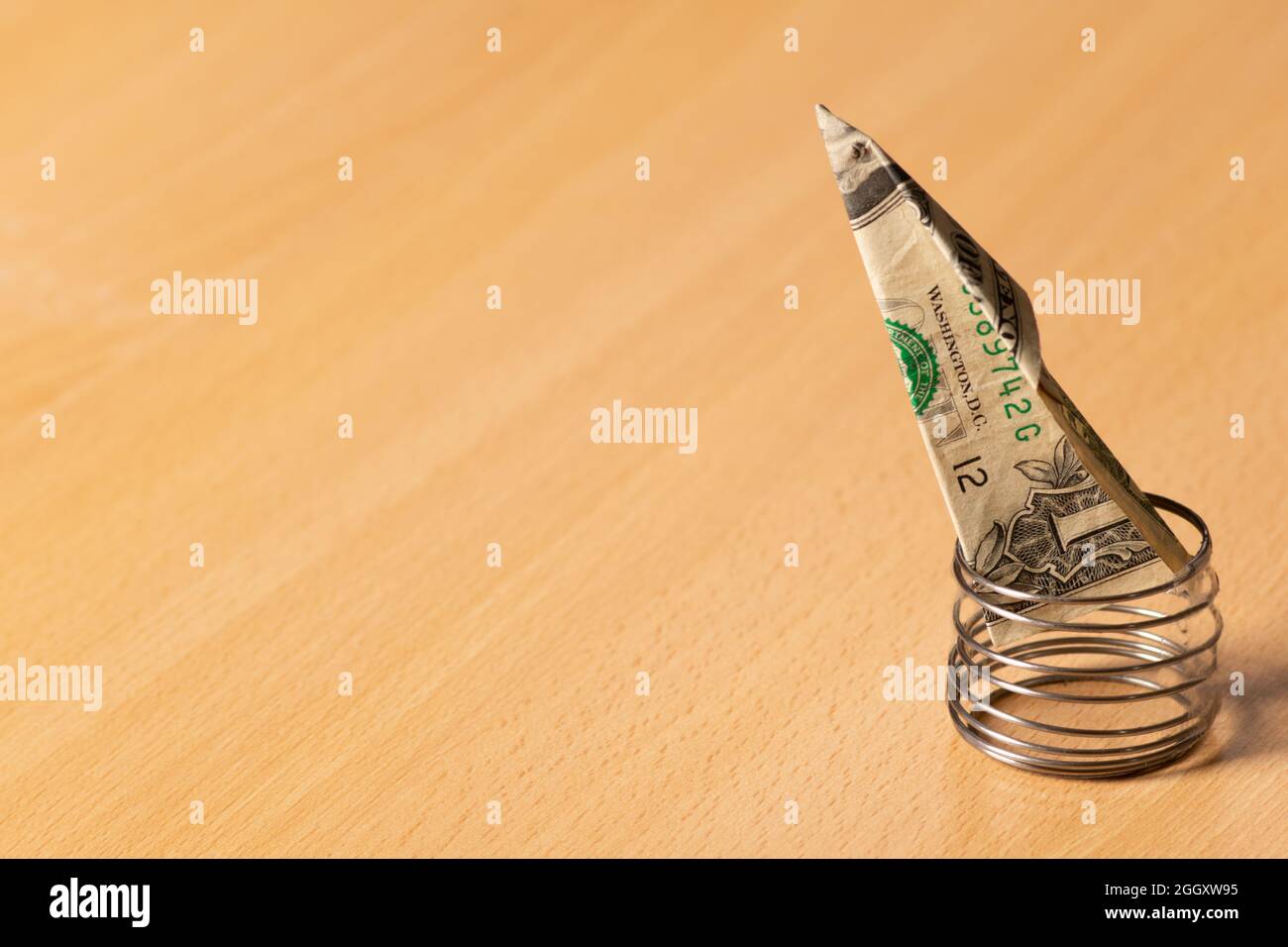 Paper plane made from dollar bill on a compressed spring on wooden ...