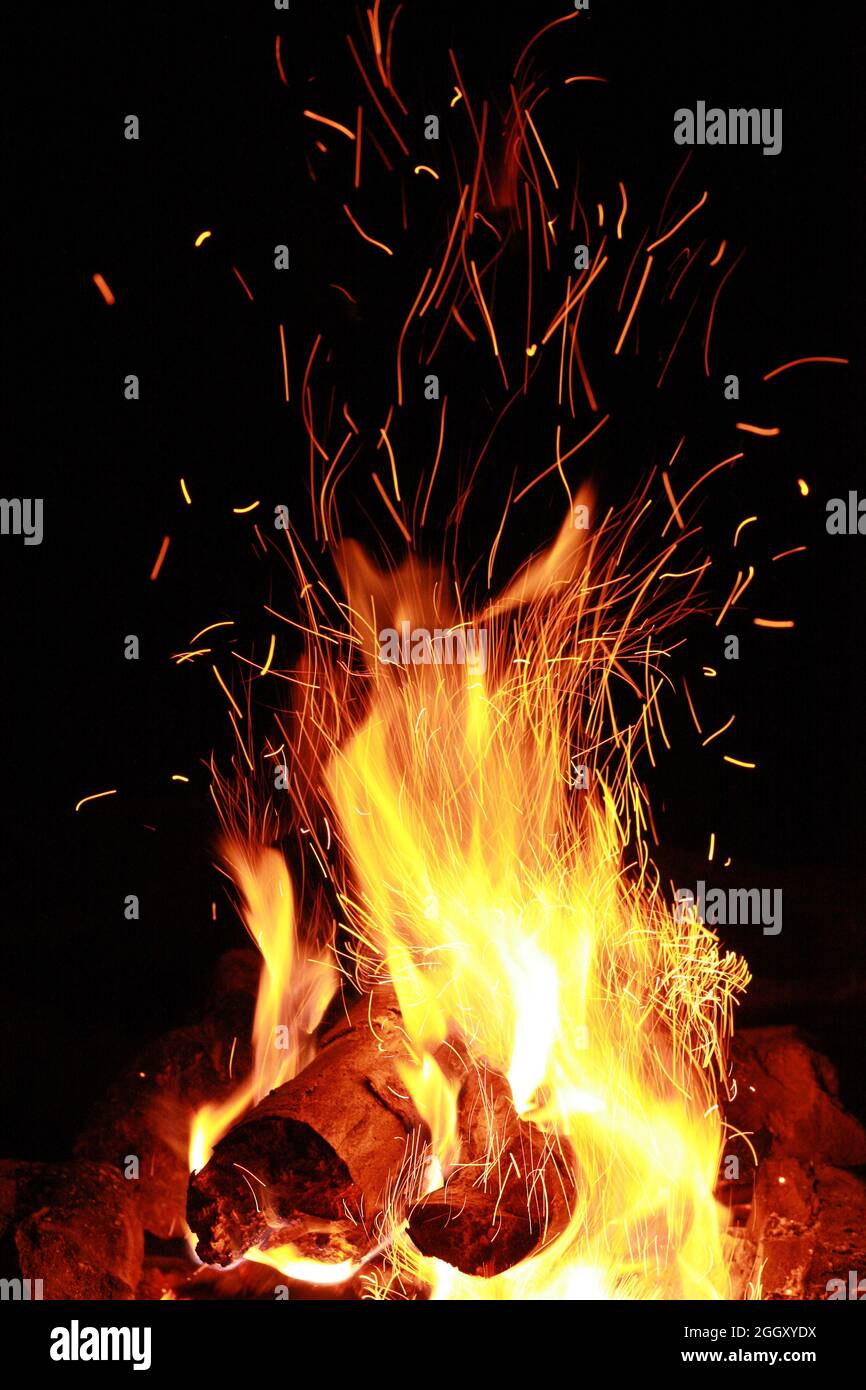 A burning fire, wooden logs, red sparks and yellow flames on a dark ...