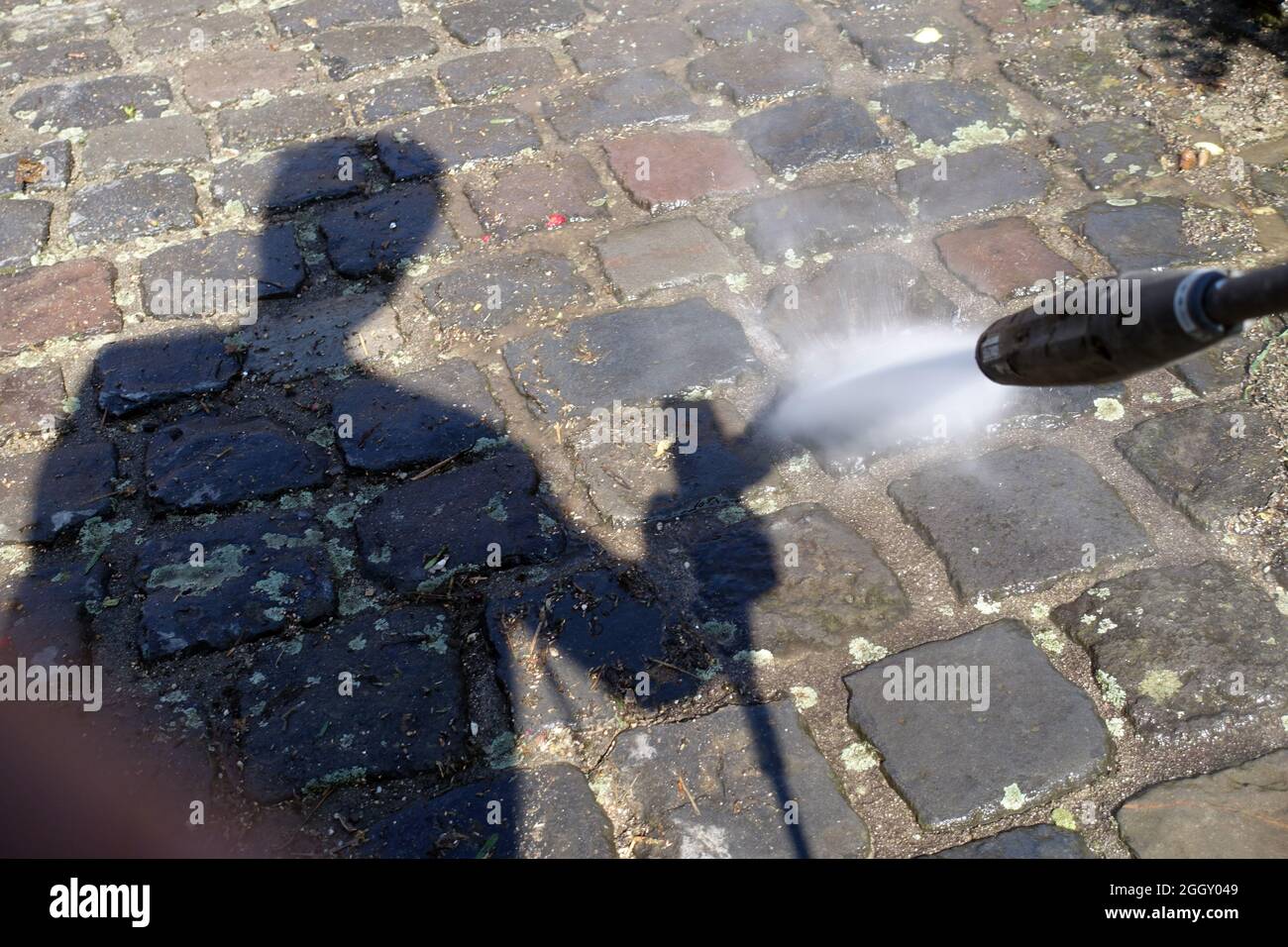 Person cleans a driveway made of basalt pavement with a pressure washer ...