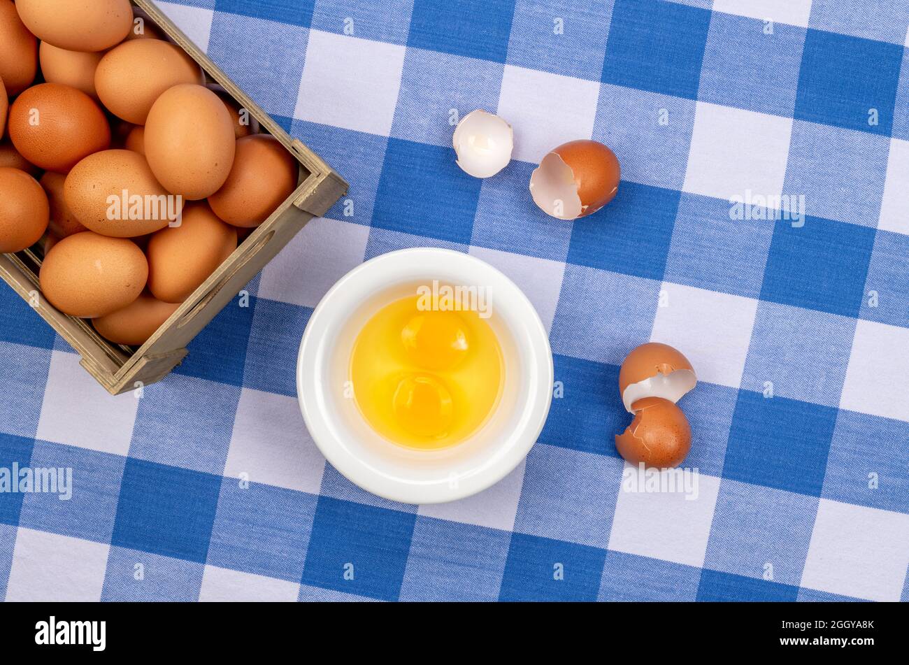 A small crate of fresh eggs with two cracked eggs rests atop a tabletop ...