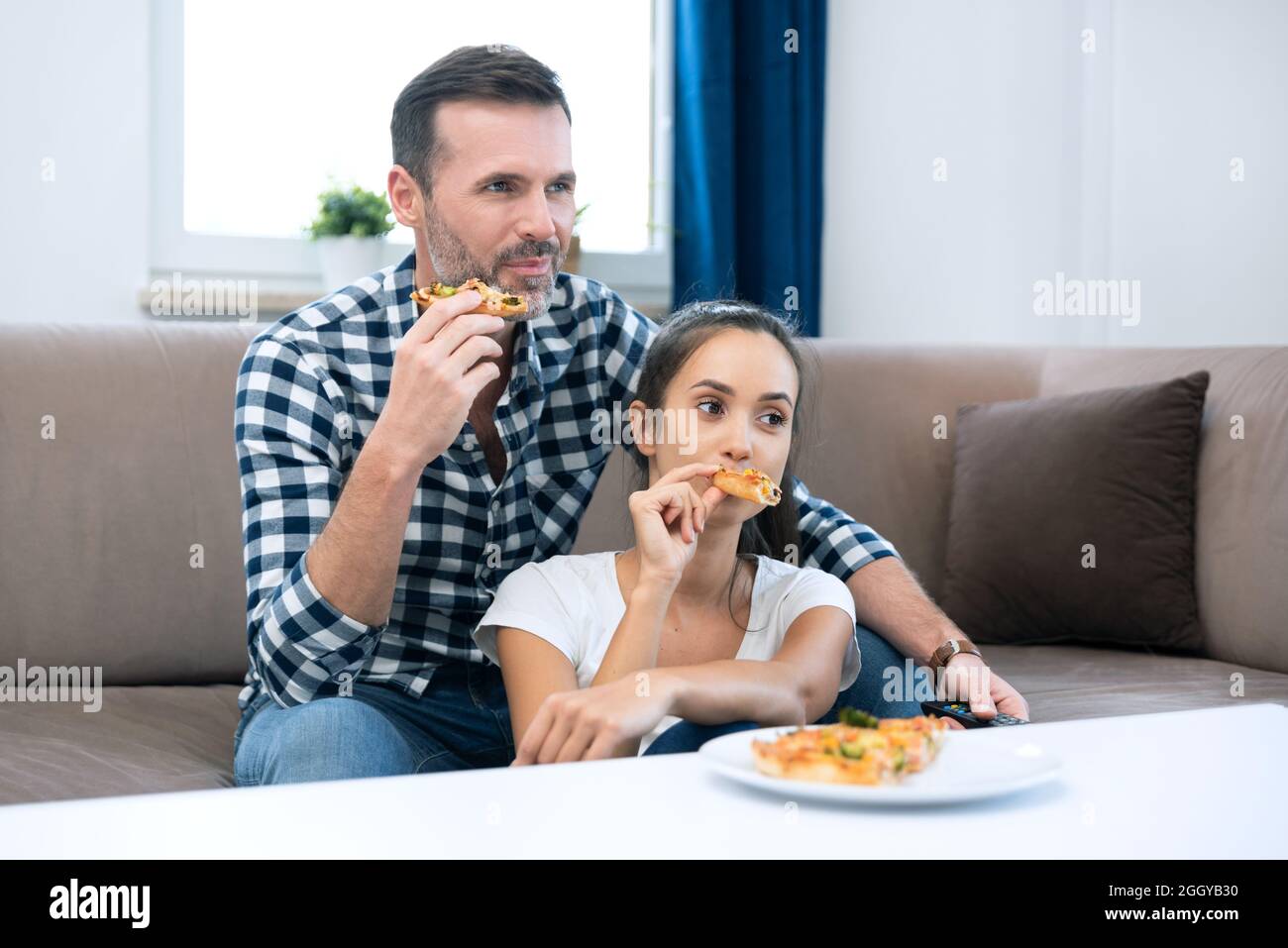 Couple watching TV while eating pizza. Spending free time at home Stock ...