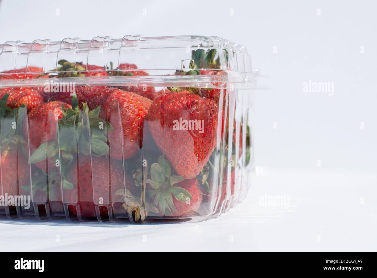 Clear plastic containers of fresh red, ripe strawberries with the stems ...