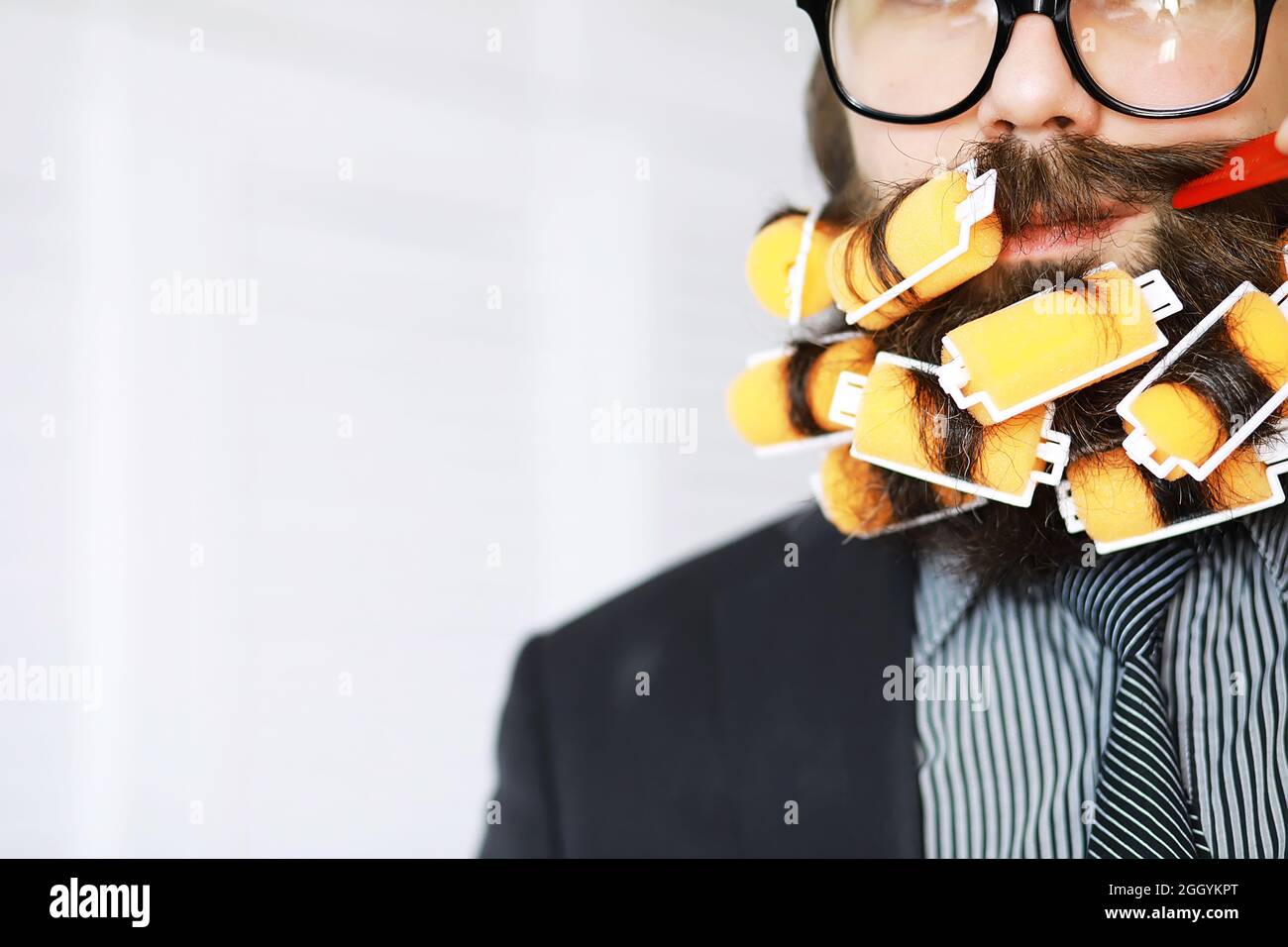 Cheerful hipster man with curlers in beard. Surprised man with glasses ...