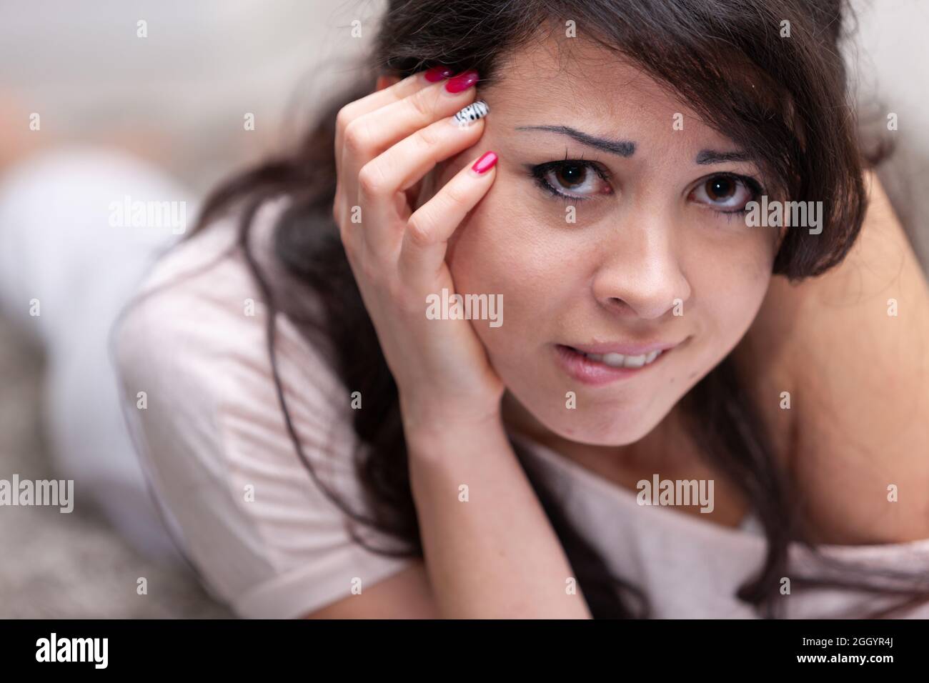 Thoughtful troubled young woman biting her lip as she gives the camera ...