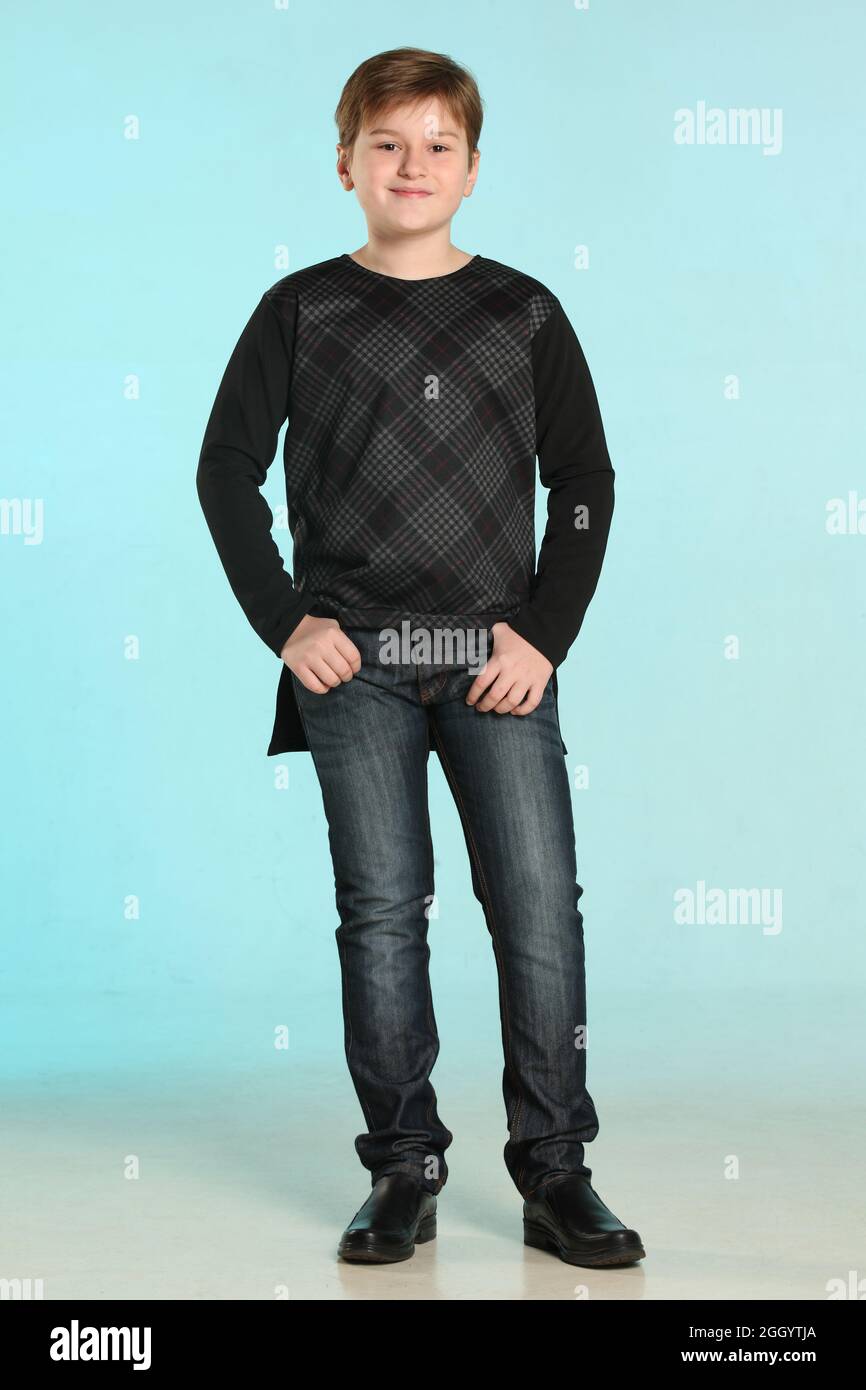 Fashionable, cheerful and considerate teenage boy slightly smiles and poses in full length in ...