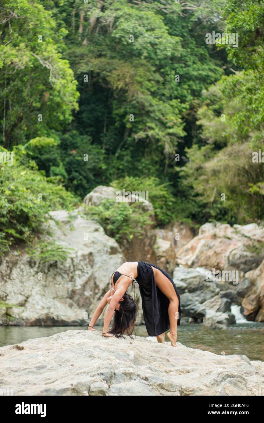 Vertical shot of a Hispanic woman doing a gymnastics pose near the lake ...