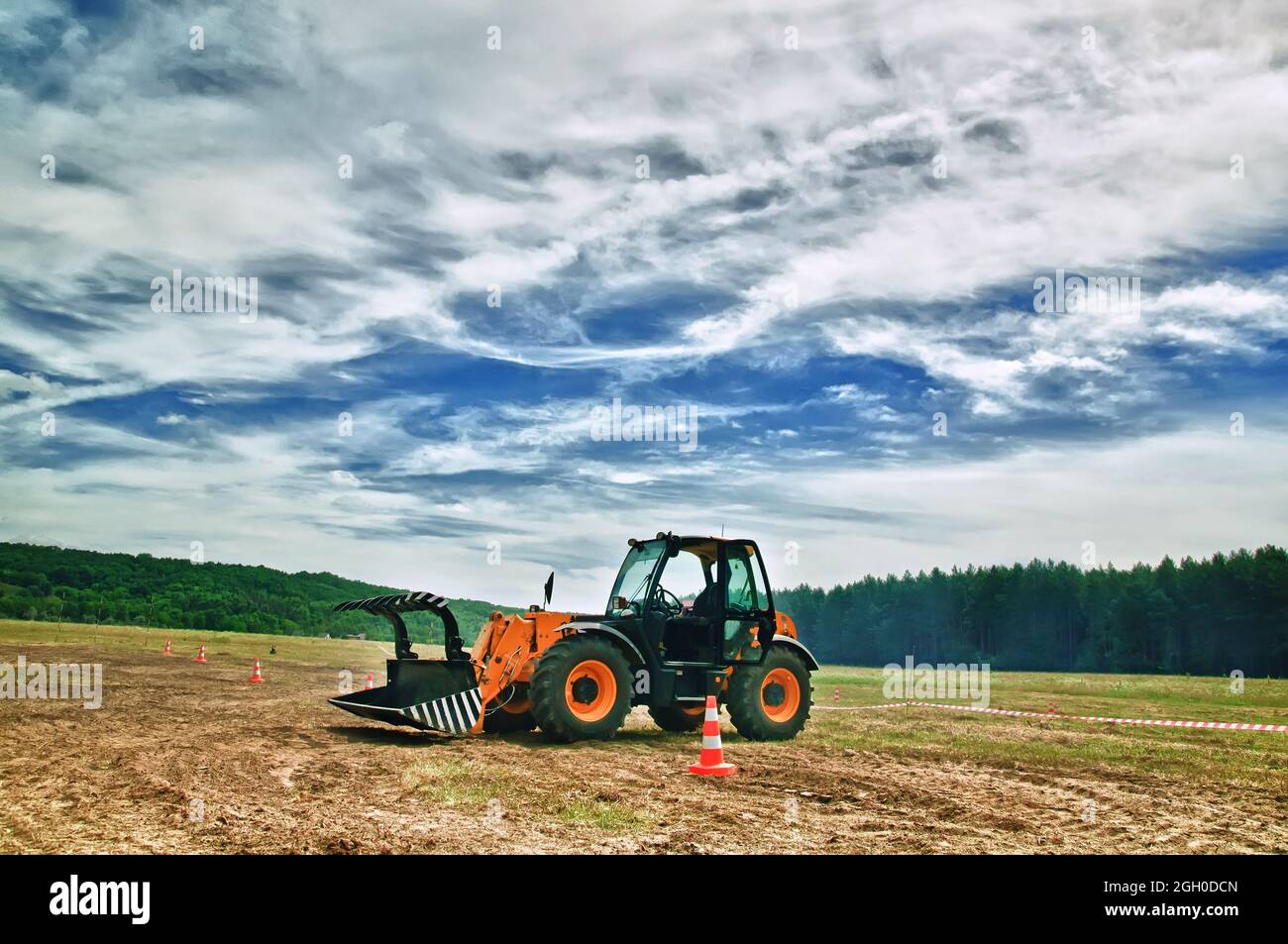 Tractor loader with a bucket in the field on forest background. Toning ...