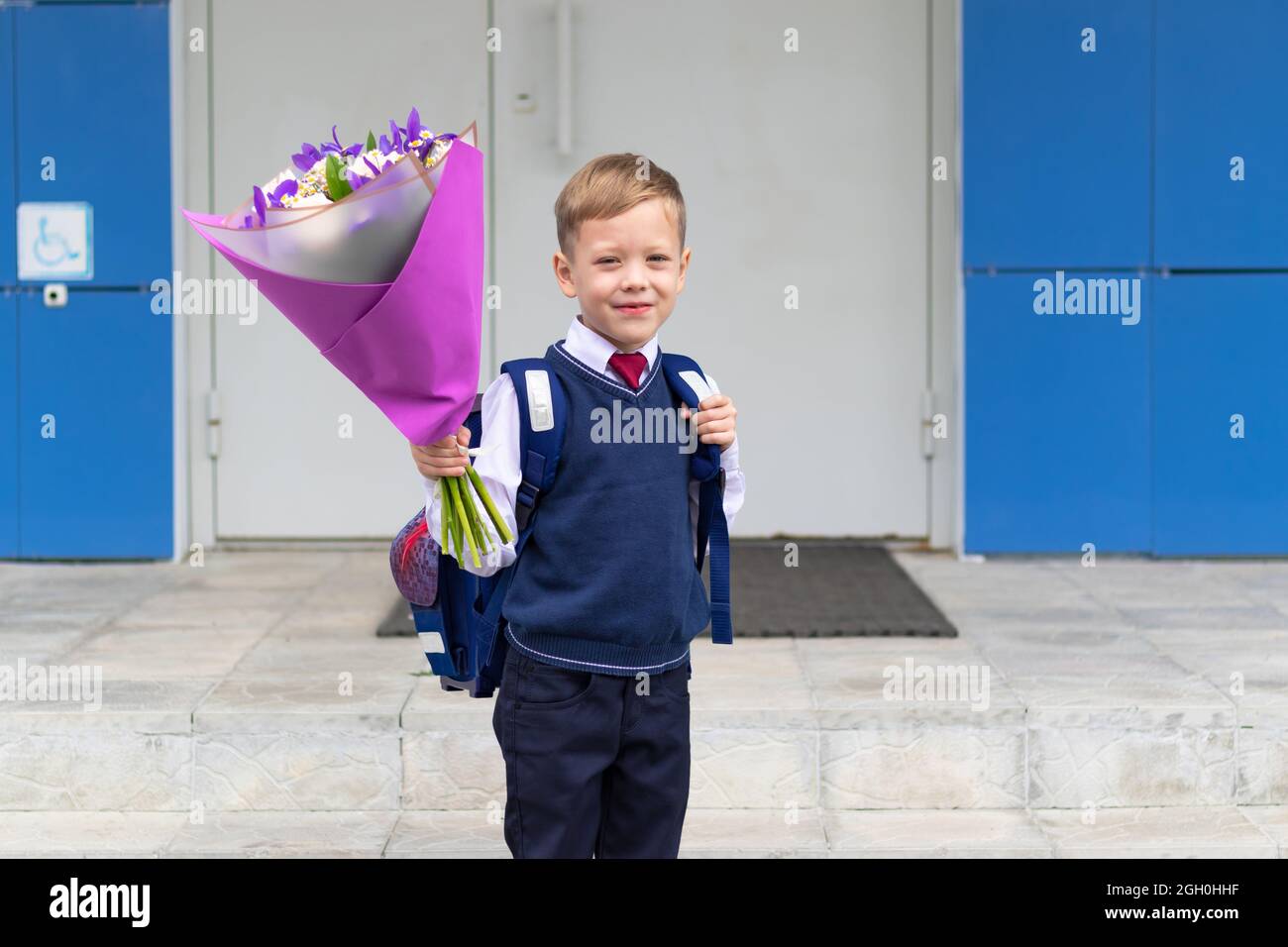A cute first-grader boy in a school uniform with a beautiful bouquet of ...