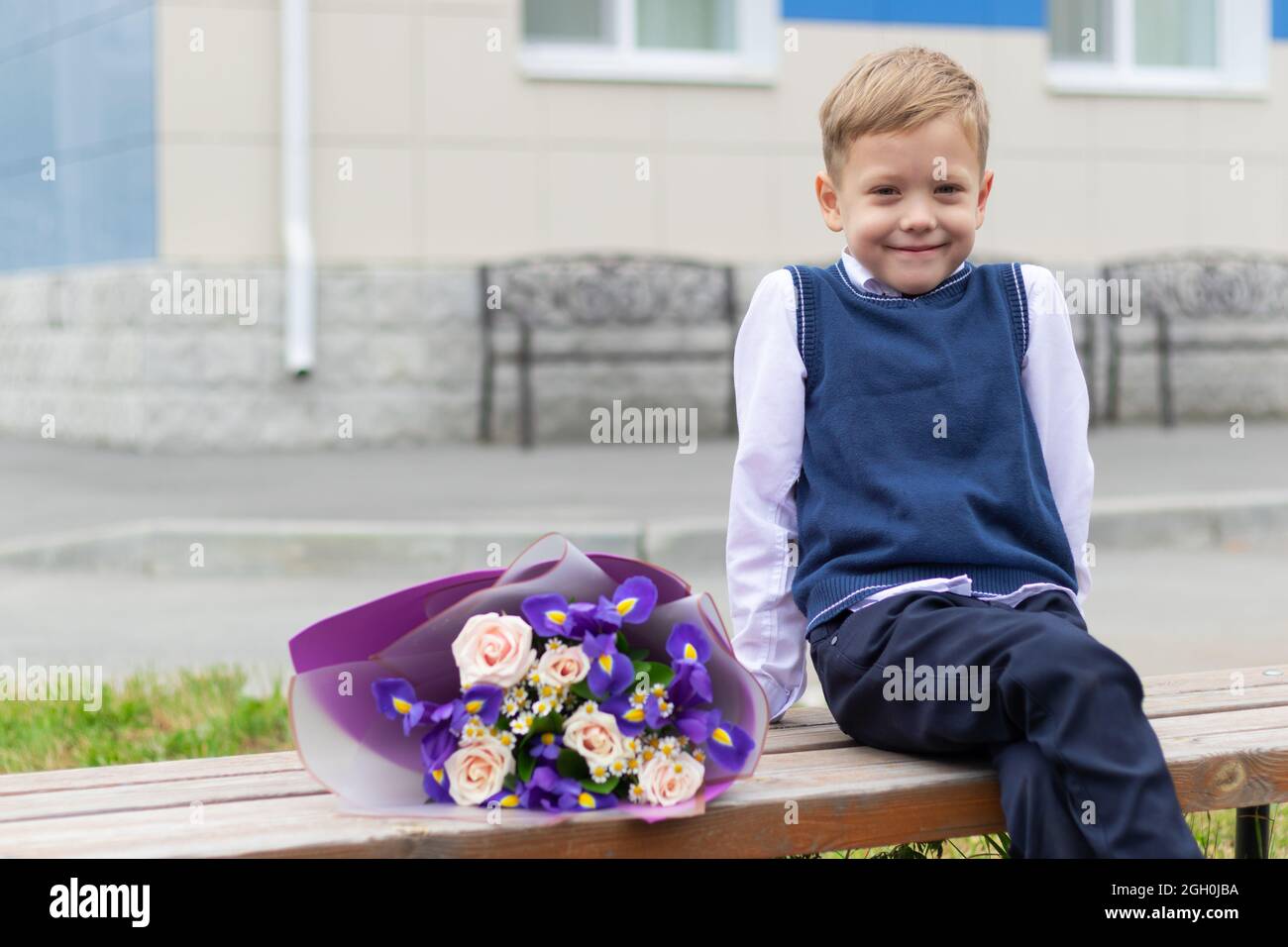 A cute first-grader boy in a school uniform with a beautiful bouquet of ...