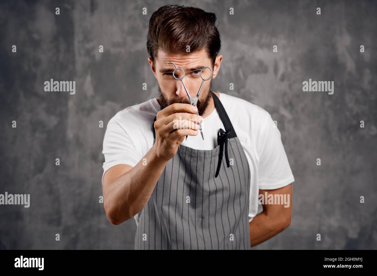 male hairdresser in an apron with a comb in his hands and scissors ...