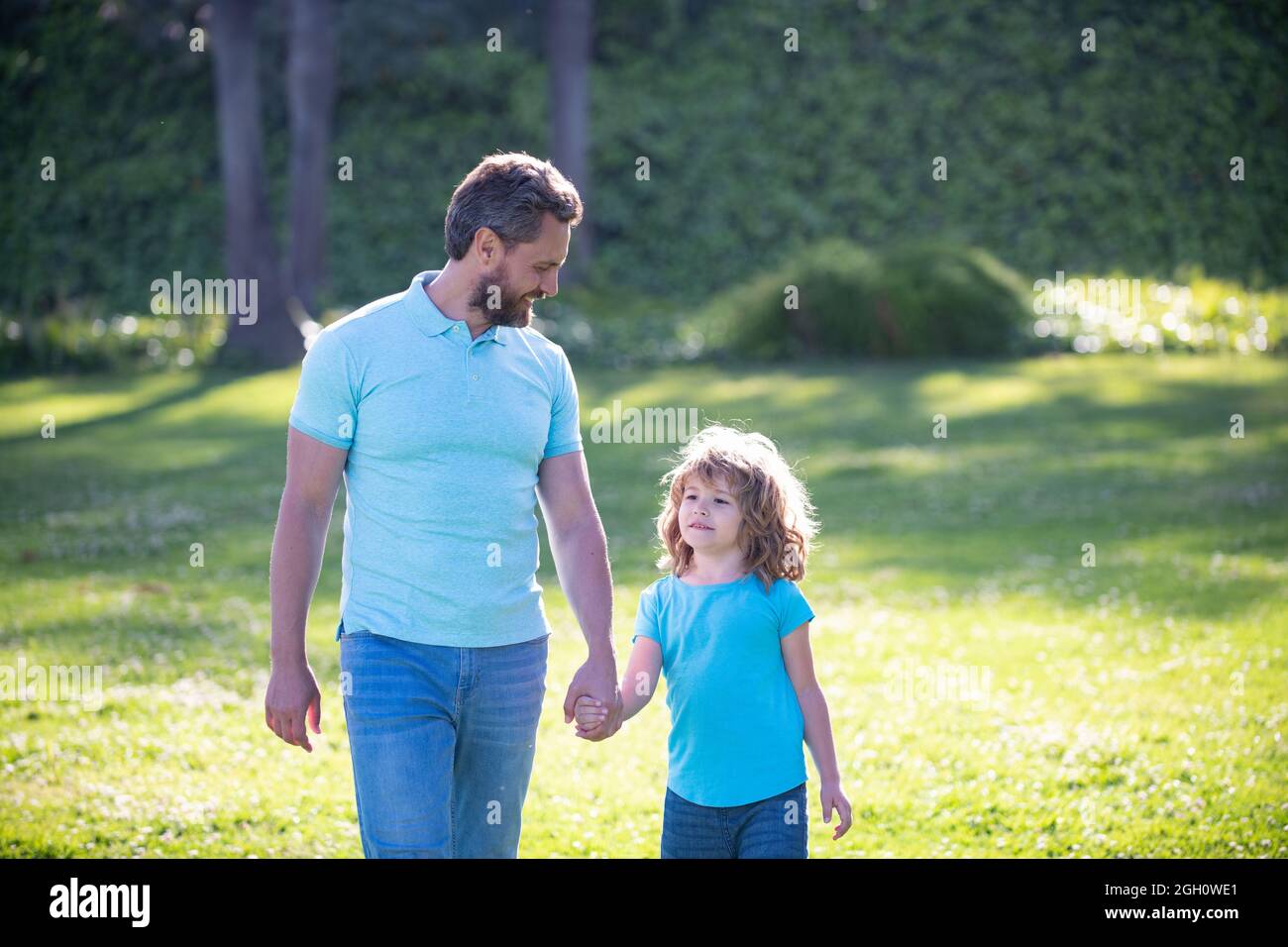 parent leads little child boy on lawn grass. dad with kid boy on summer ...