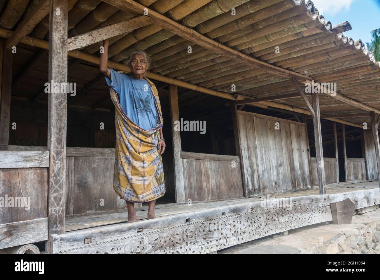 Old woman on the verandah of a wooden house in the traditional village ...