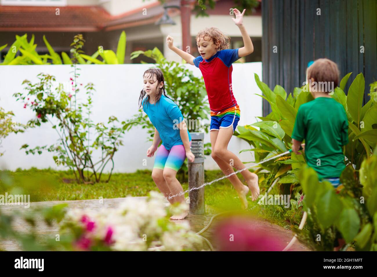 Kids playing with water hose in summer garden. Child water sprinkler ...