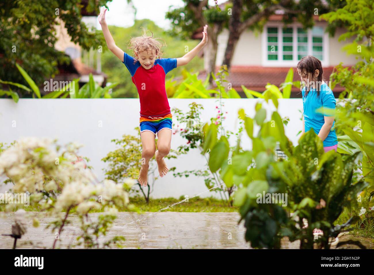 Kids playing with water hose in summer garden. Child water sprinkler ...