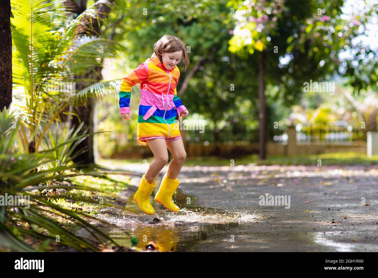 Kid playing in the rain in autumn park. Child jumping in muddy puddle ...