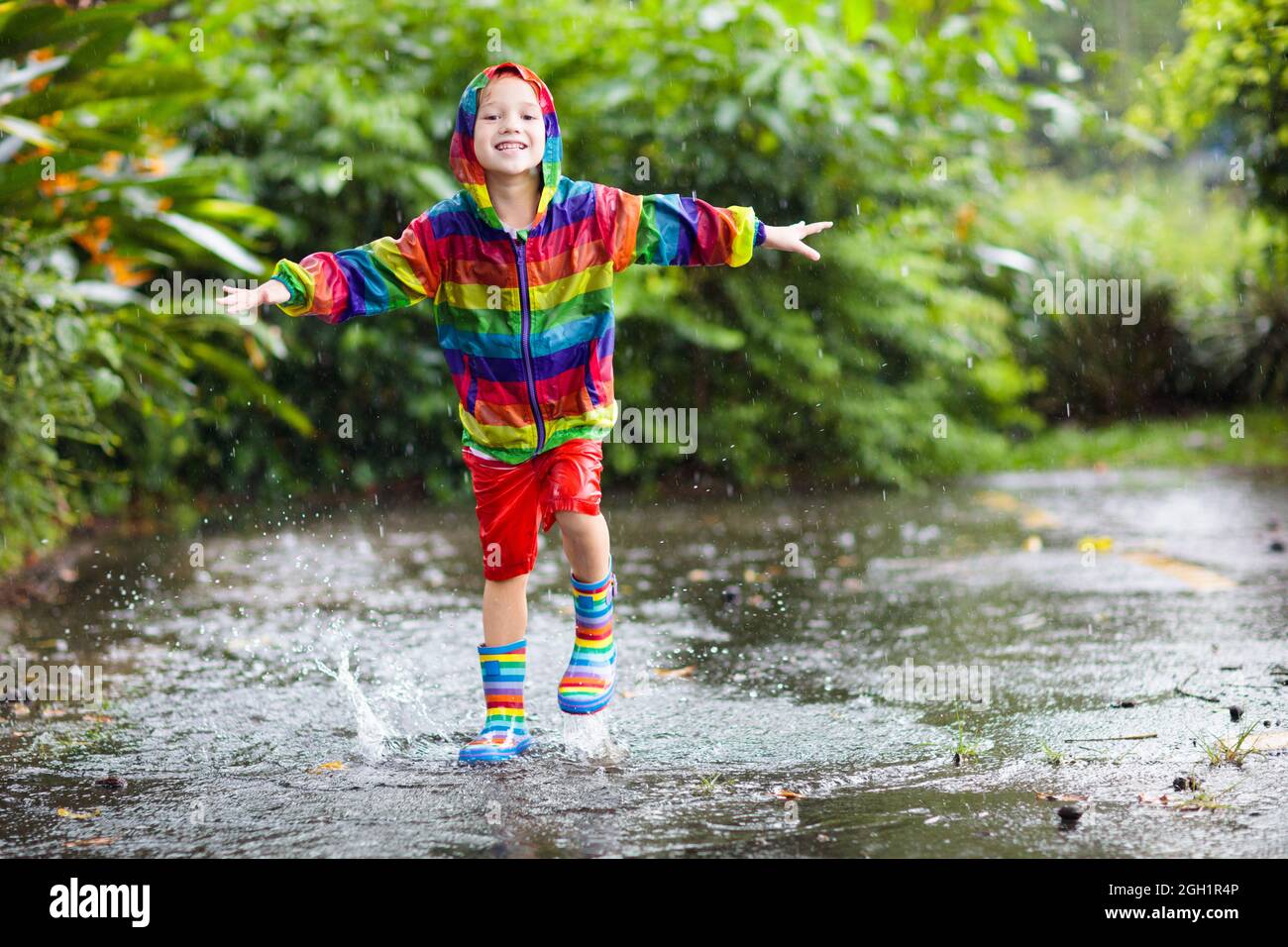 Kid playing in the rain in autumn park. Child jumping in muddy puddle ...
