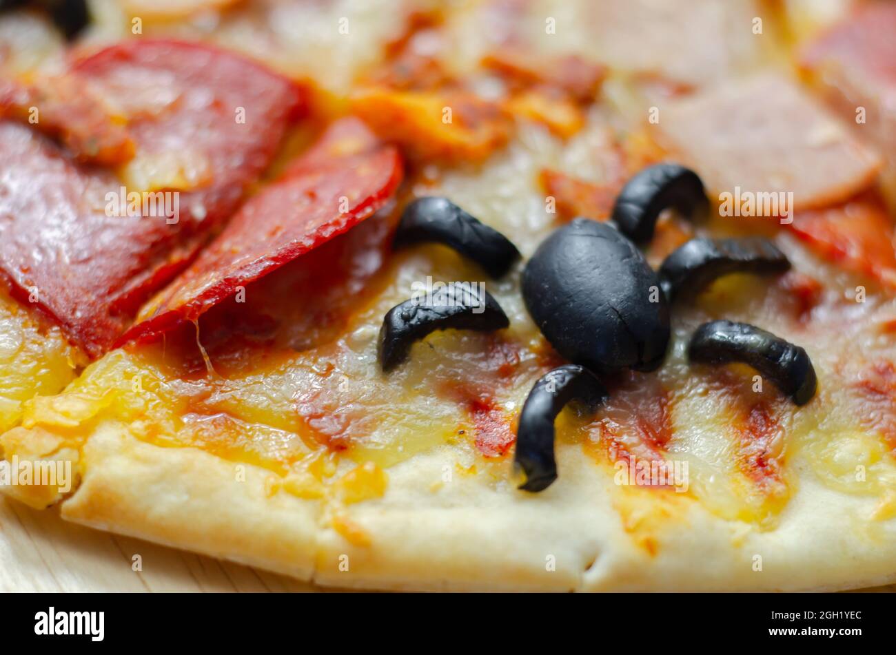 Meat feast pizza on thin dough decorated with black olives in the shape ...