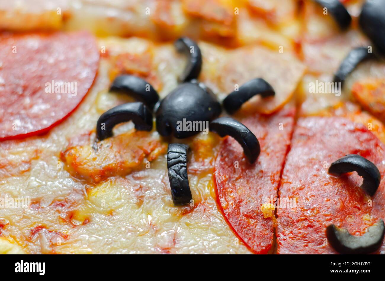 Meat feast pizza on thin dough decorated with black olives in the shape ...