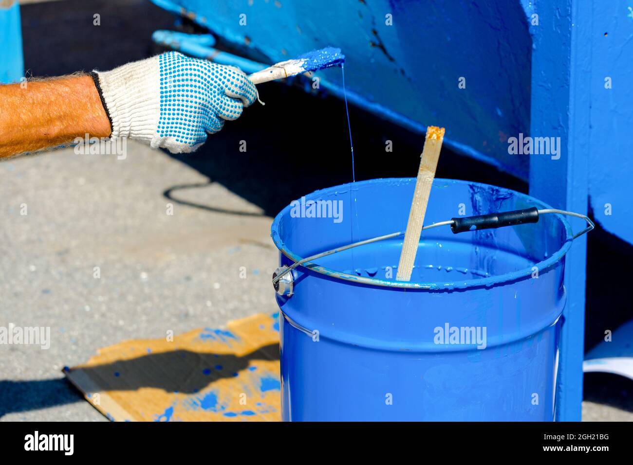 Metal bucket with blue paint. A hand in a protective glove holds a ...