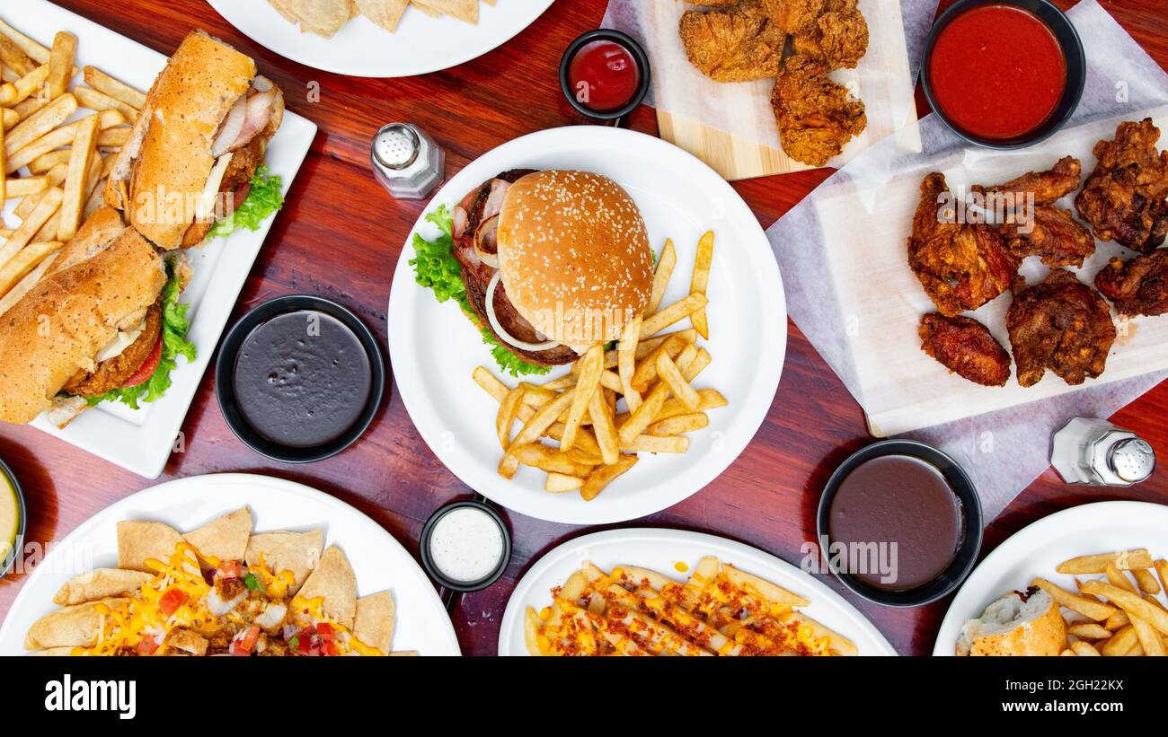 Top shot of a table with burgers, fries, chicken wings, salads, and ...